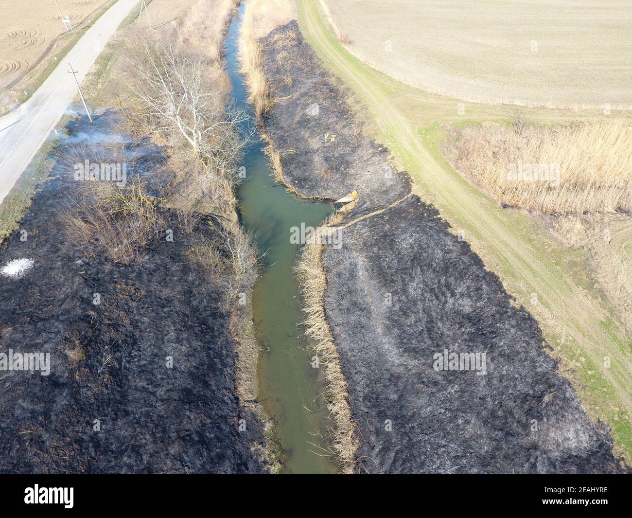 Burning dry grass along the irrigation canal. Smoke and the flame of ...