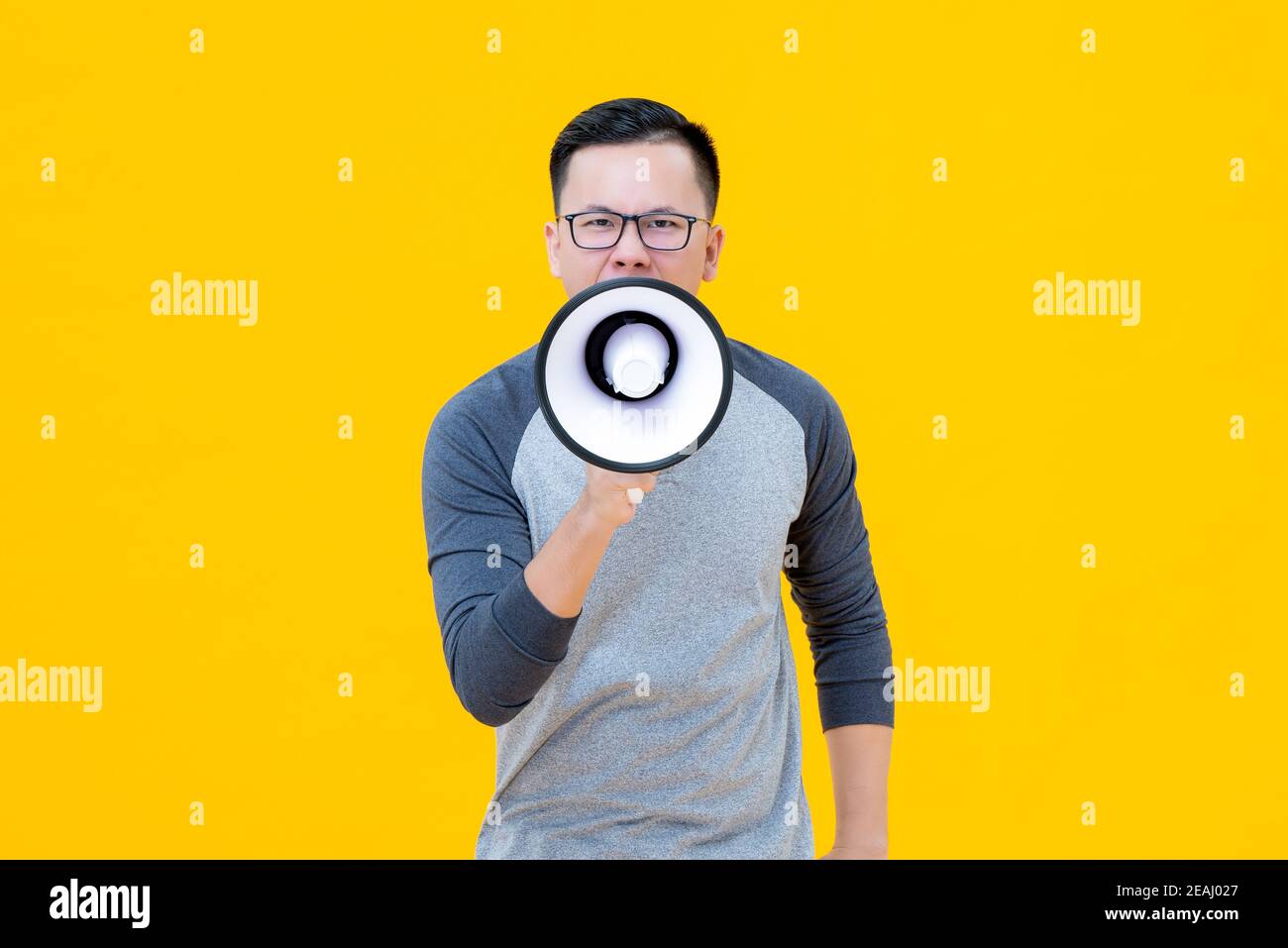 Asian Chinese man shouting on megaphone isolated on yellow studio ...