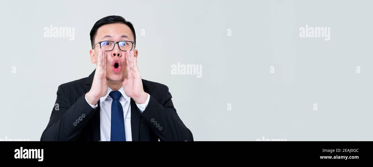 Excited young Asian businessman shouting with hands cupped around mouth ...