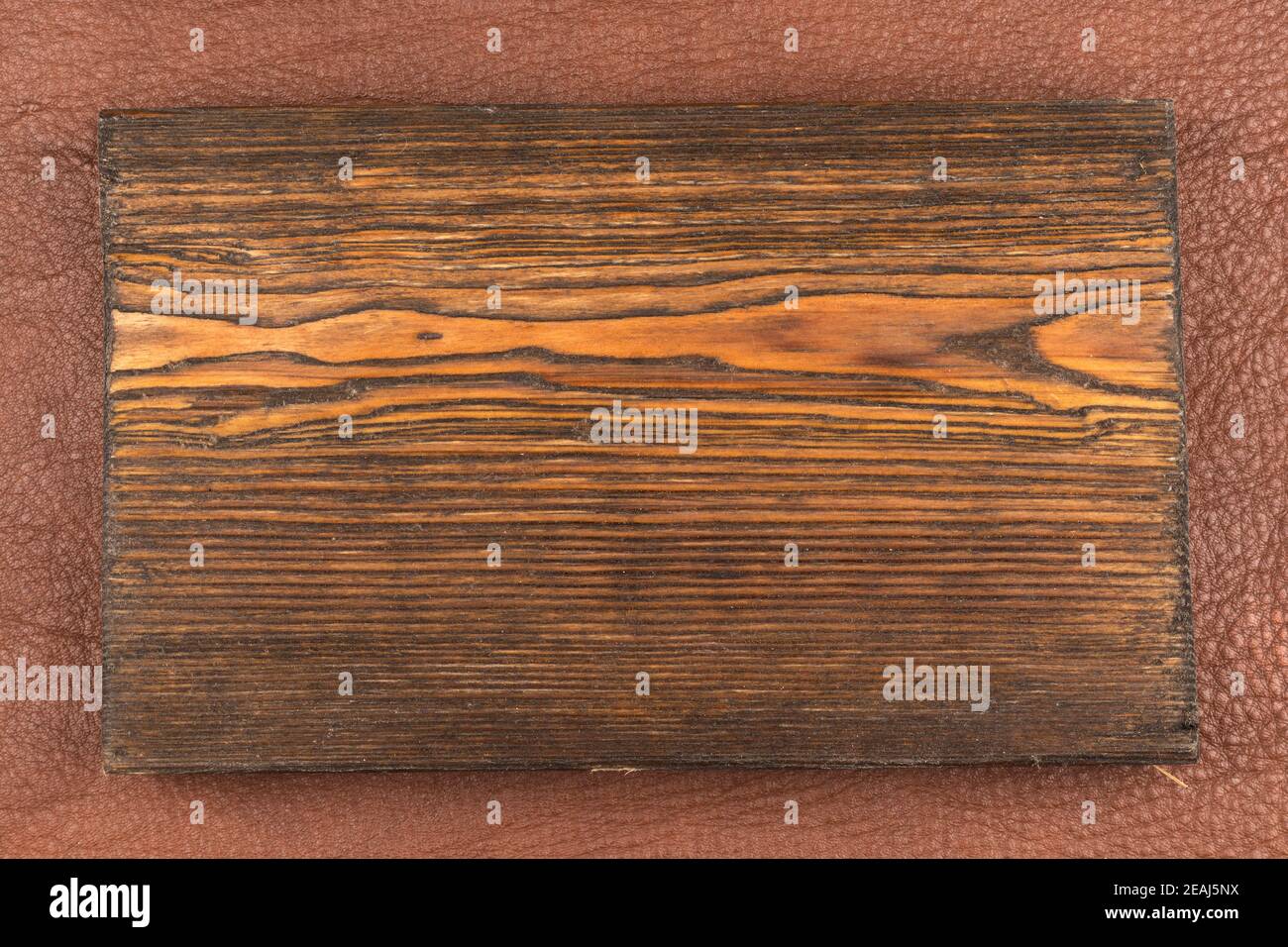 Rectangular board of dark wood lies on brown natural leather. Texture ...