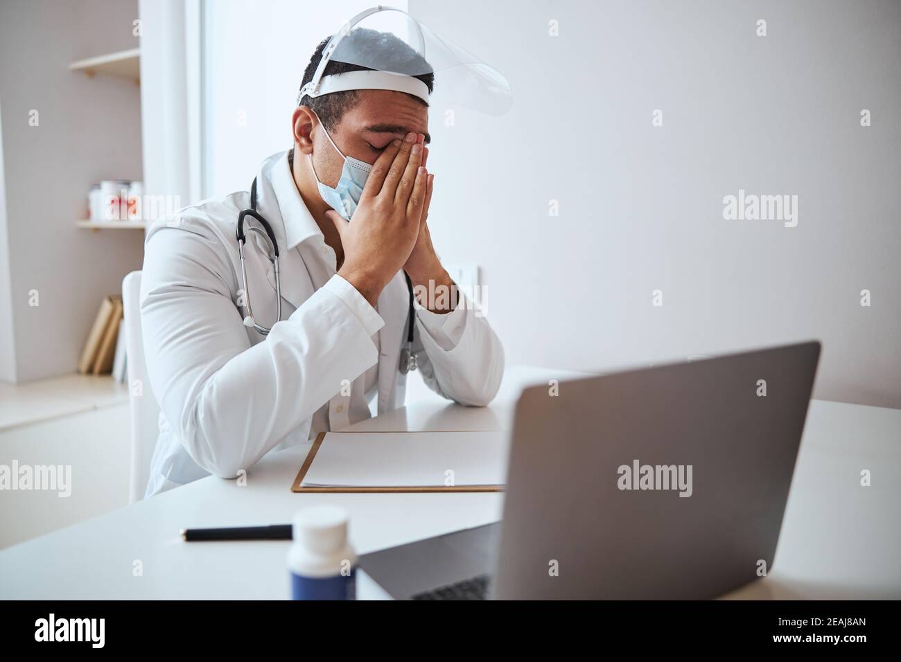 Handsome tired doctor in white uniform sitting at the work desk while ...