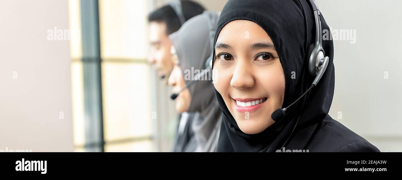 Smiling Asian muslim woman wearing microphone headsets working as ...