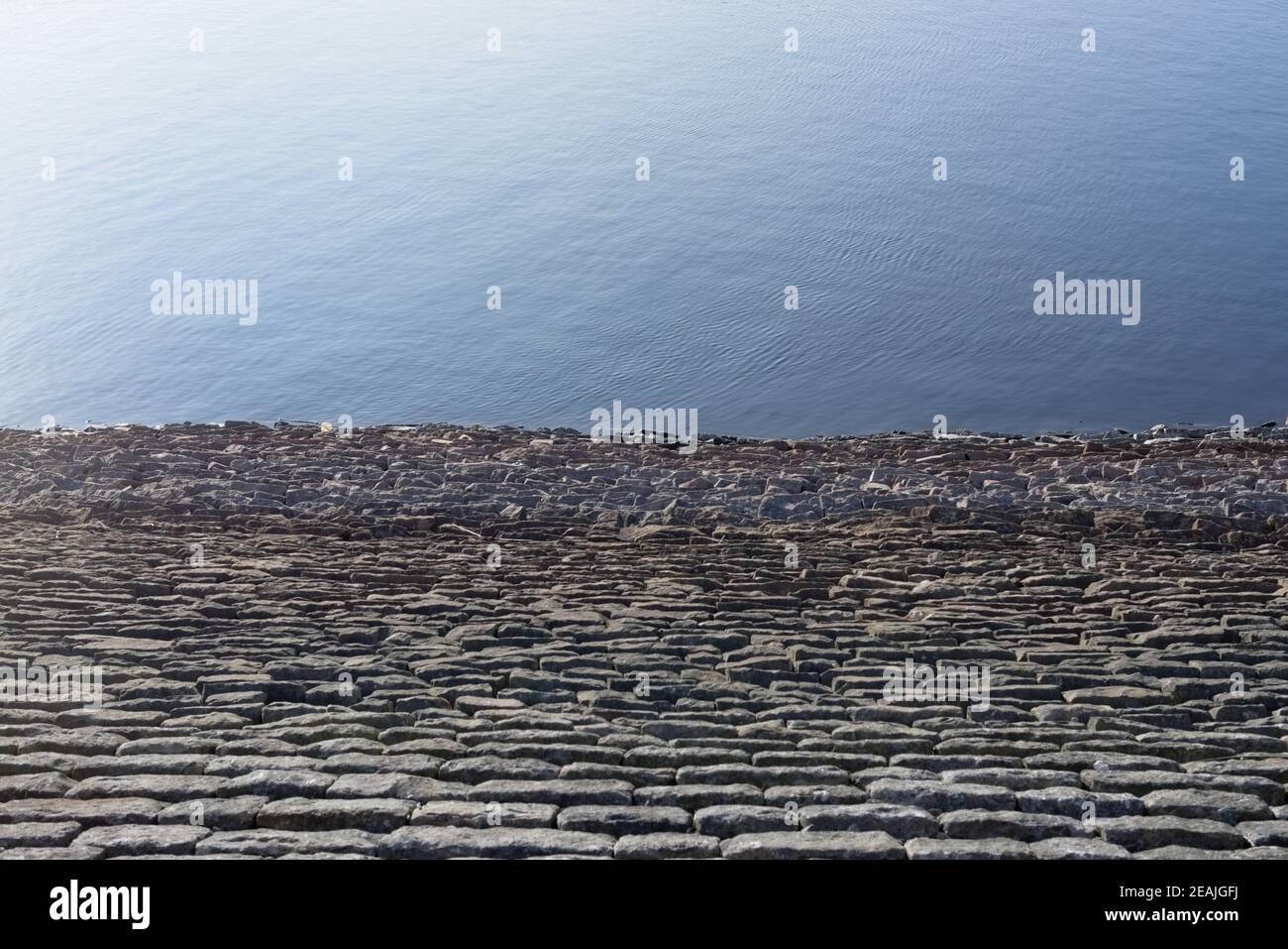 Half bright sunny blue water and half stone reservoir wall texture ...