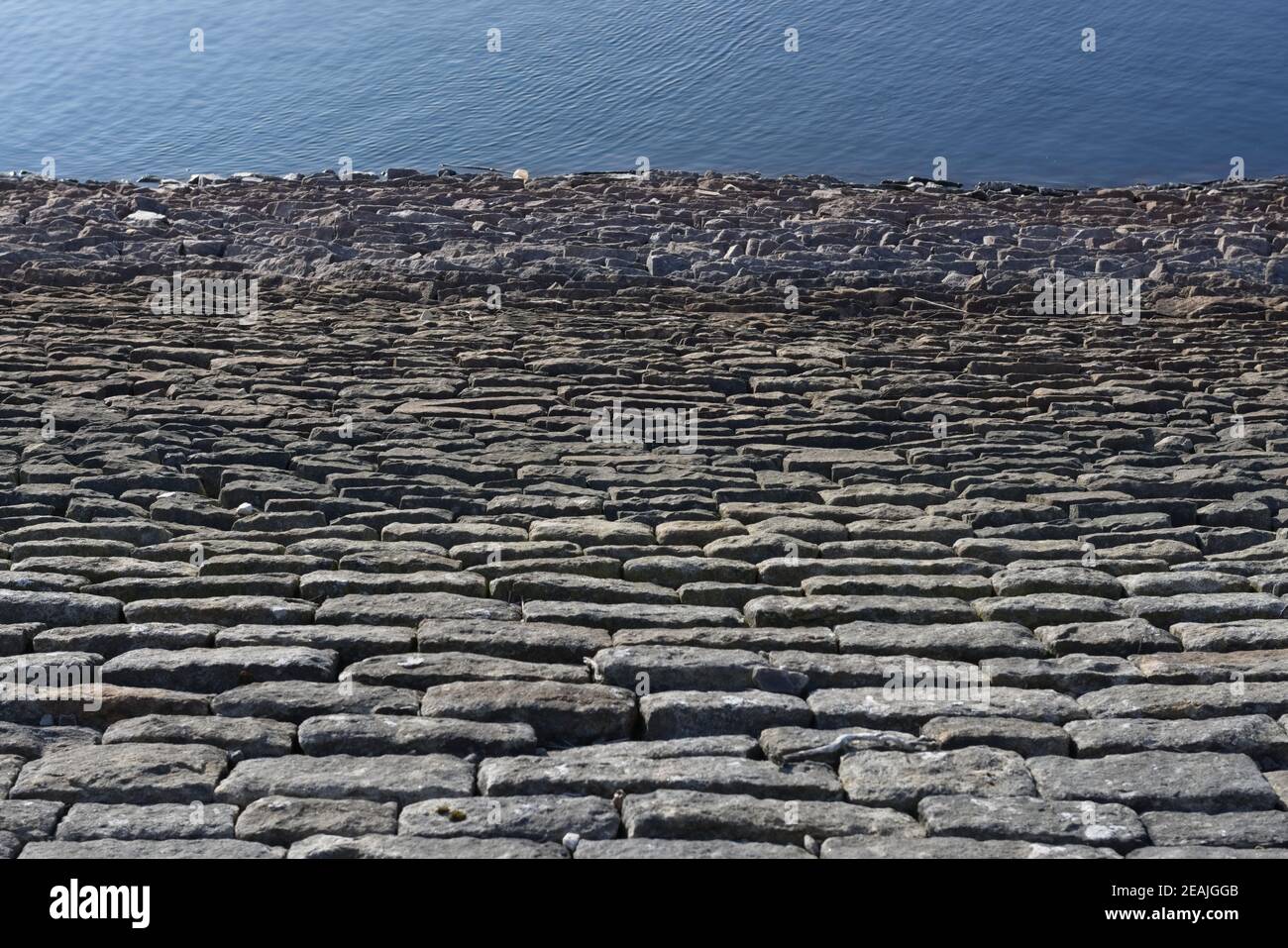 Abstract dam wall, looking down towards deep blue water, sunny stones ...