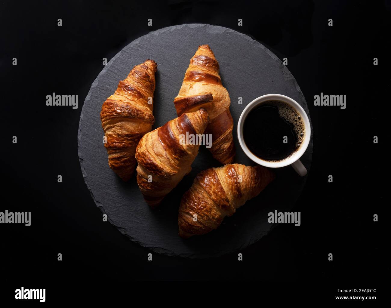 Croissants and hot coffee on a black stone plate with a black ...