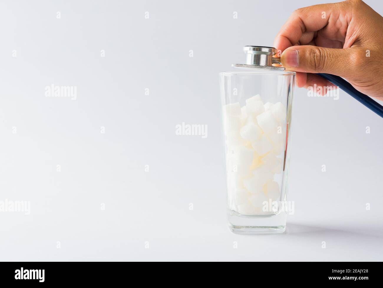 Hand of doctor hold stethoscope check on glass full of white sugar cube ...