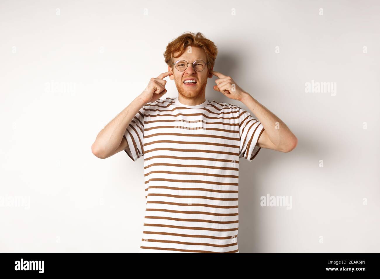 Annoyed redhead guy in glasses shutting ears and complaining loud noise ...