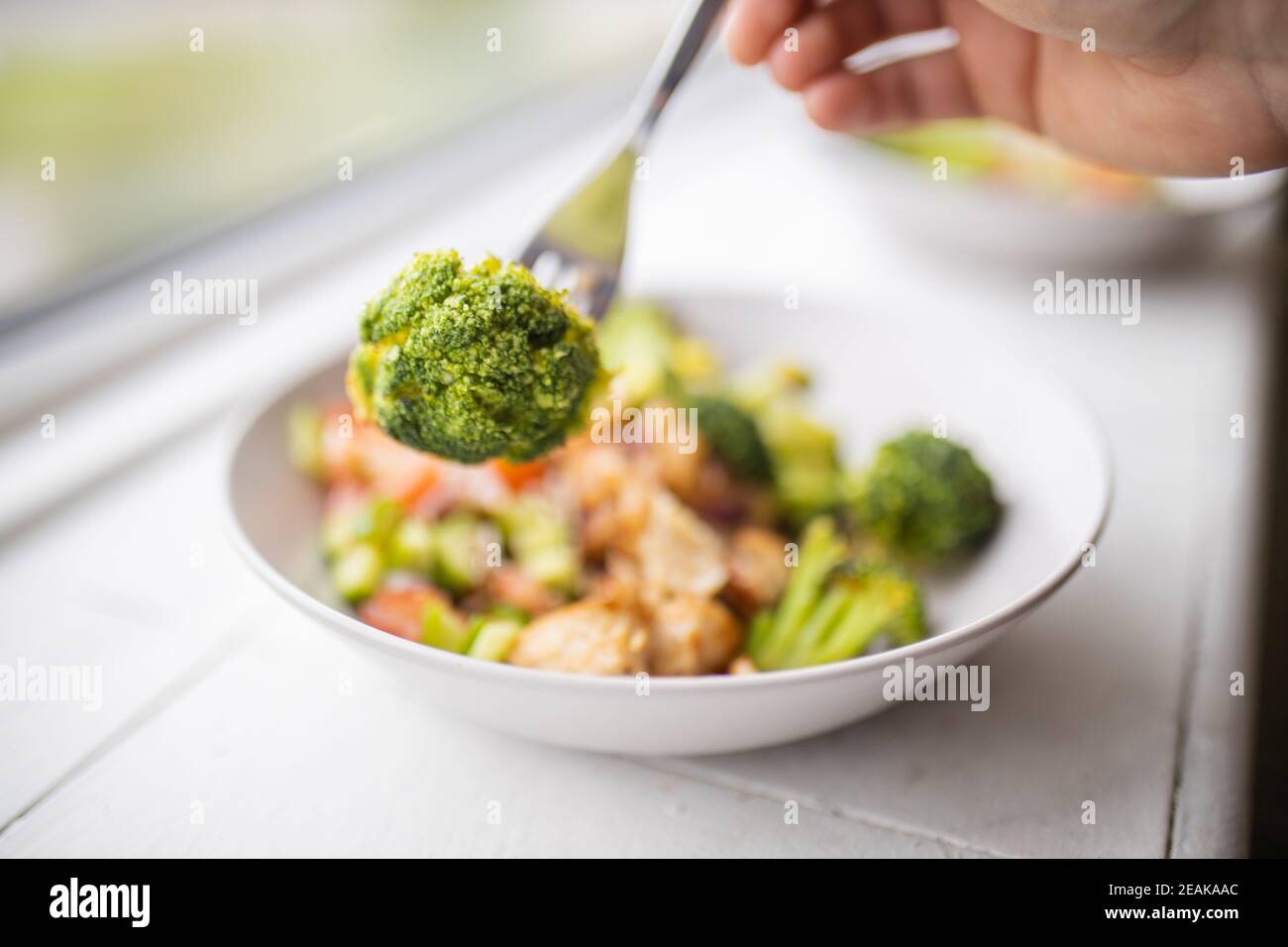 Fork picking broccoli from a broccoli and chicken salad next to a ...