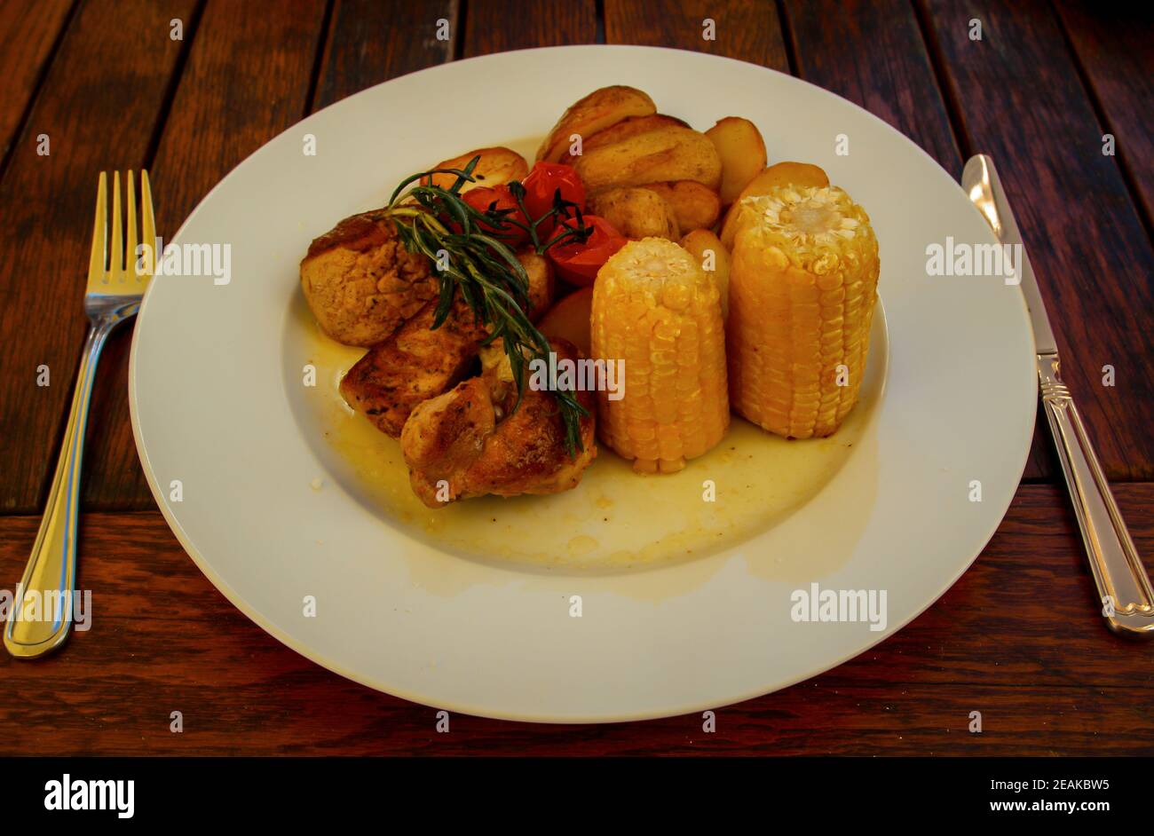 Fried pork fillets on a plate with corn on the cob and tomatoes Stock ...