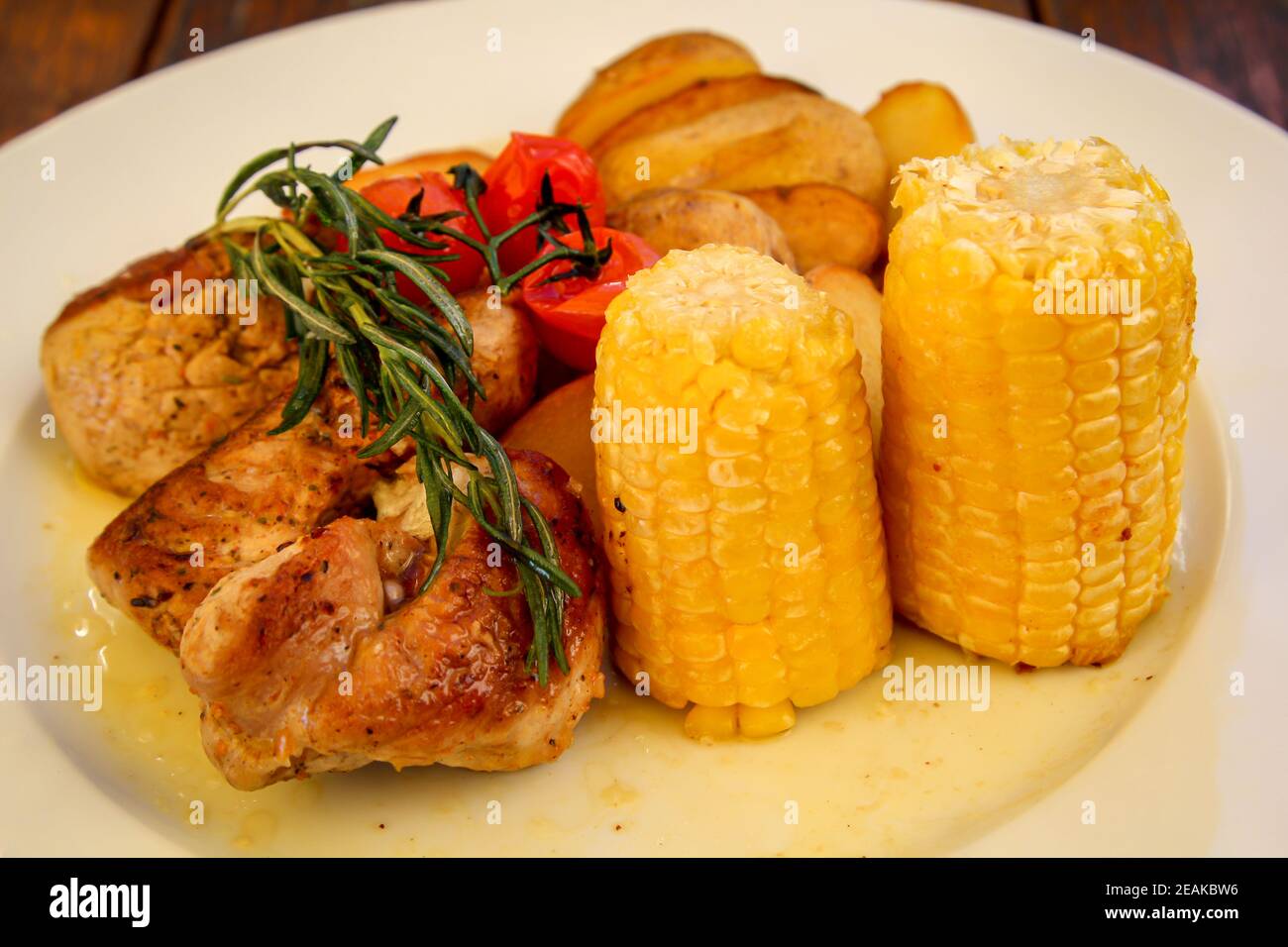 Fried pork fillets on a plate with corn on the cob and tomatoes Stock ...