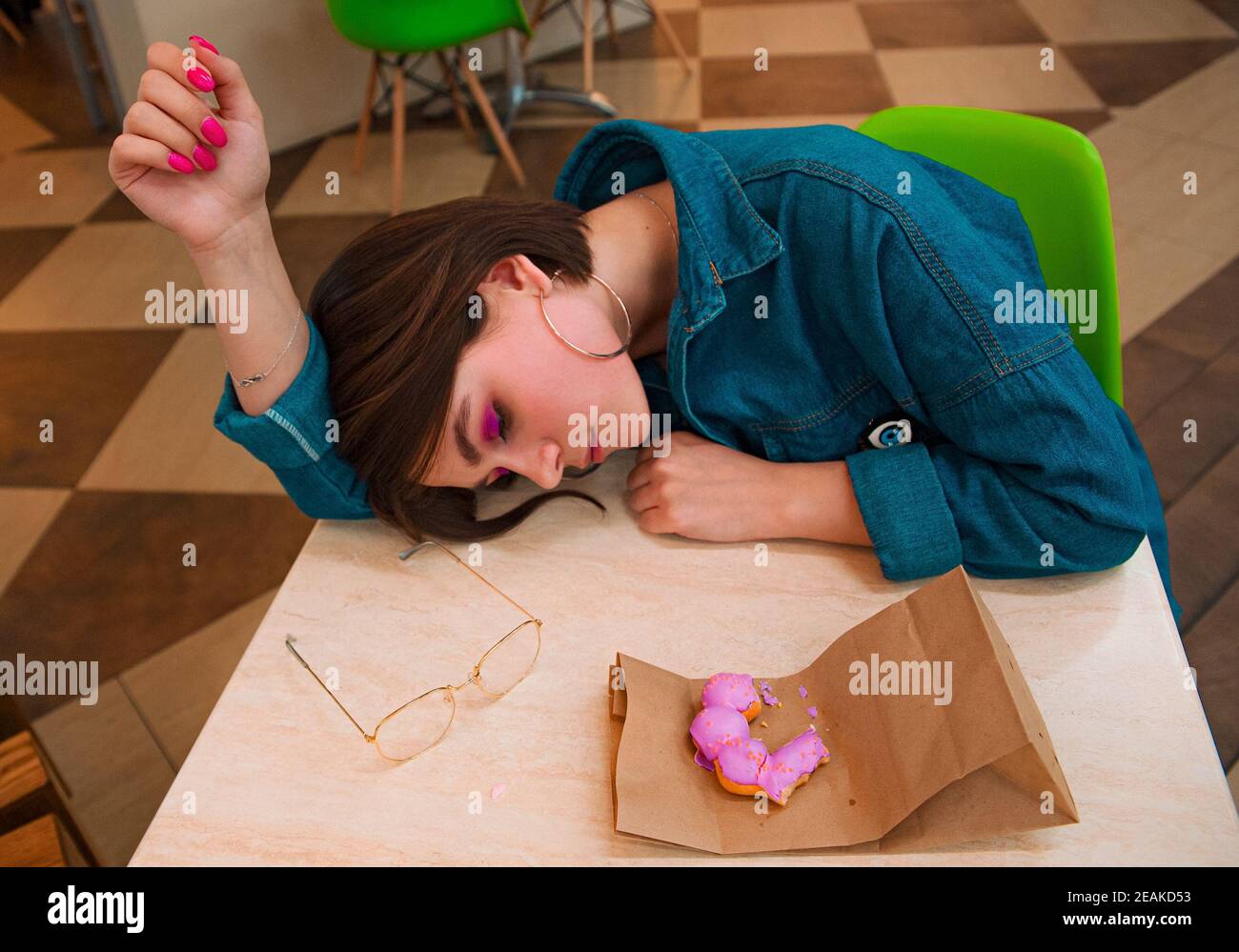 A girl eats a doughnut in a shopping center, leaning on a table Stock ...
