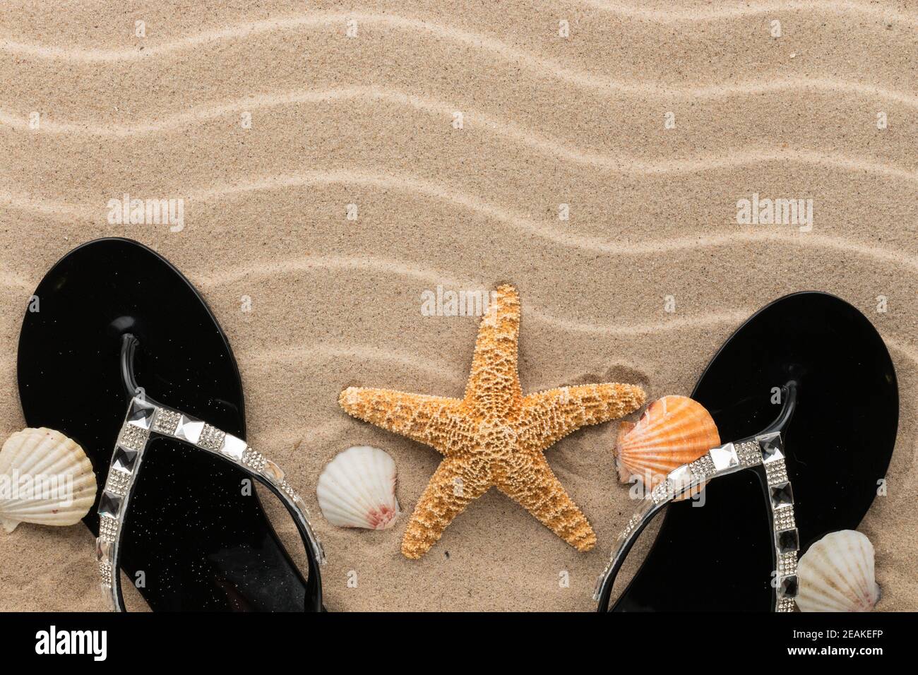Beach fashion, black flip-flops and starfish standing in the sand beach ...