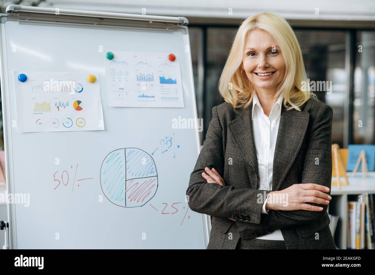 Friendly mature business woman stands in modern office near flipchart ...