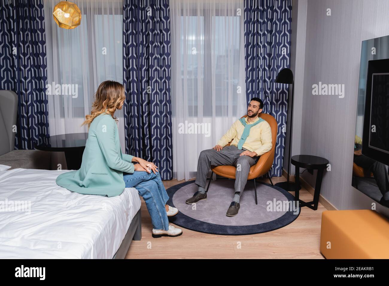 Smiling arabian man sitting on armchair near girlfriend on bed in hotel ...