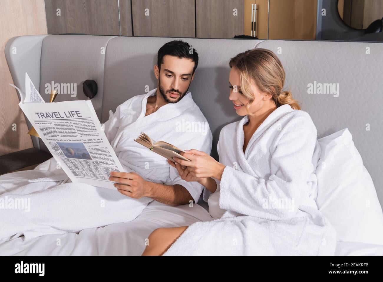 Smiling woman showing book to muslim boyfriend with newspaper on hotel ...