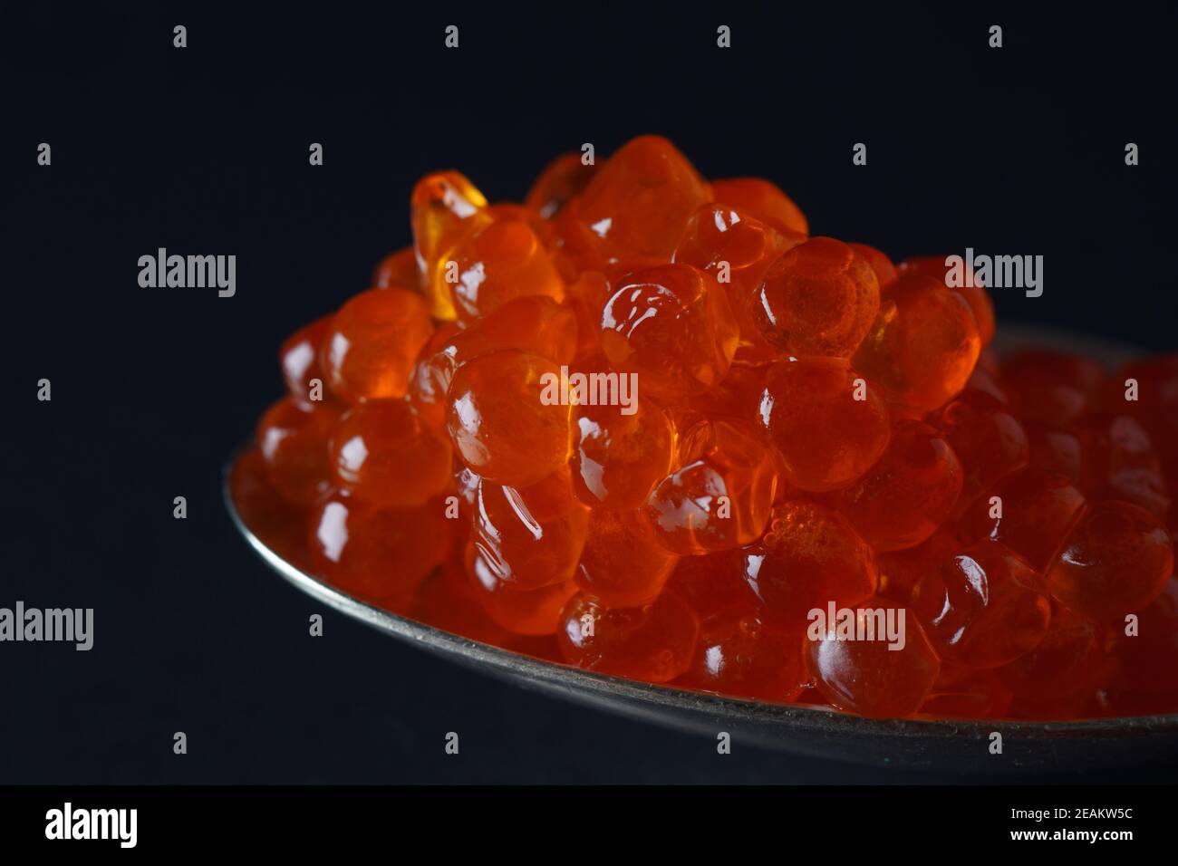 Red Caviar in a spoon over black background. Close-up salmon caviar ...