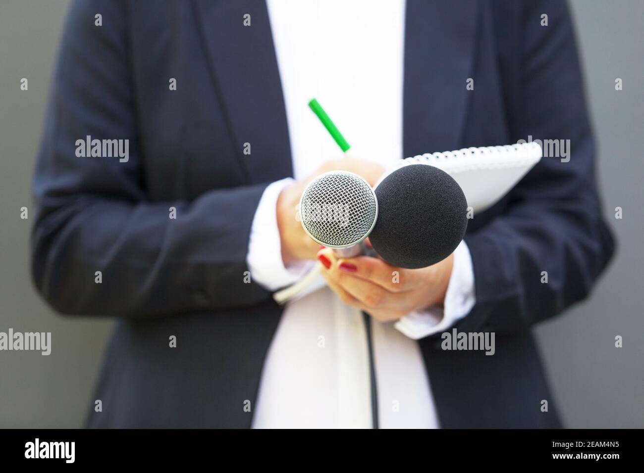 Female journalist at news conference, writing notes, holding microphone ...