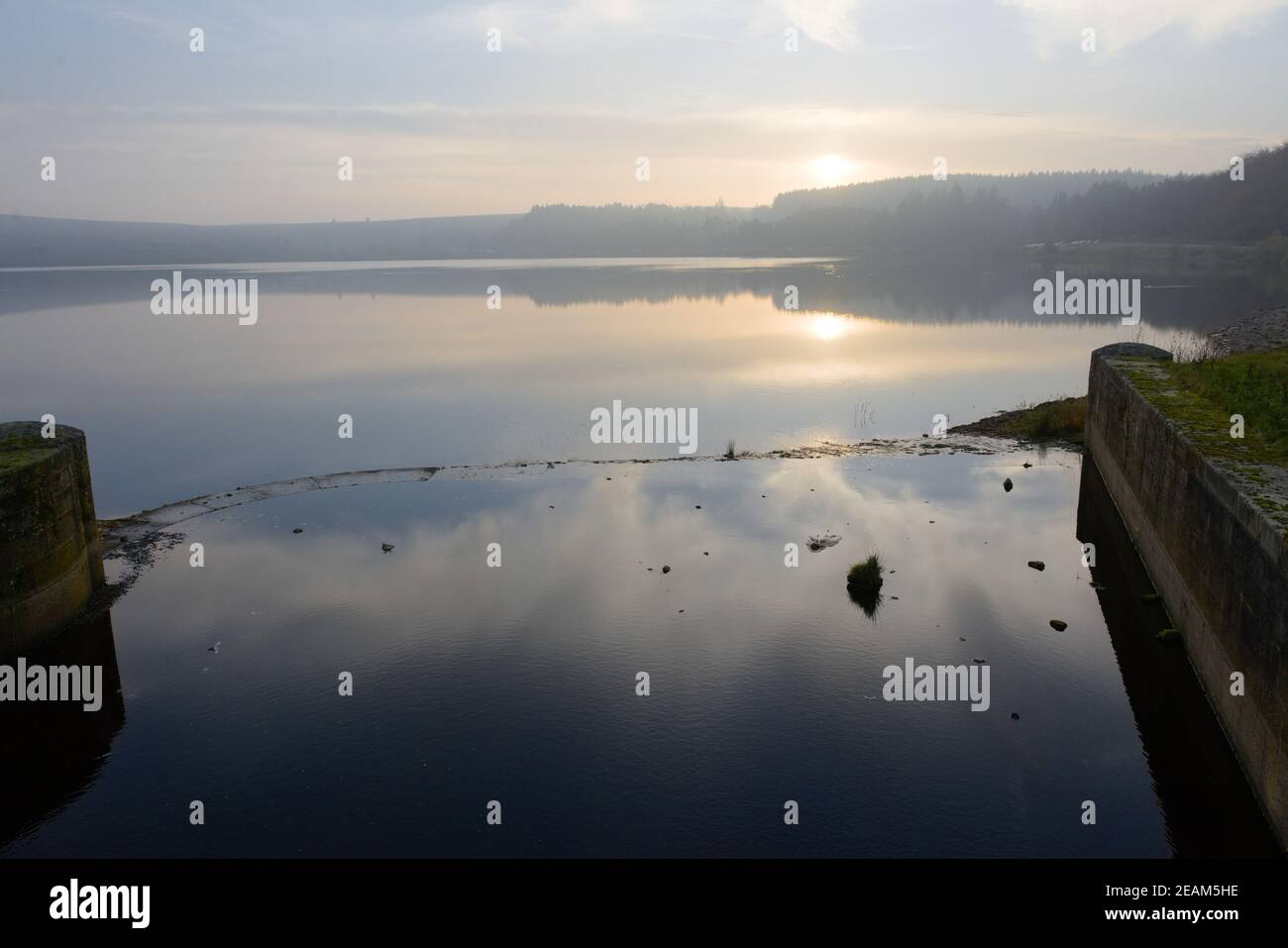 Redmires reservoir dam inlet overflow reflecting a misty water sunset ...