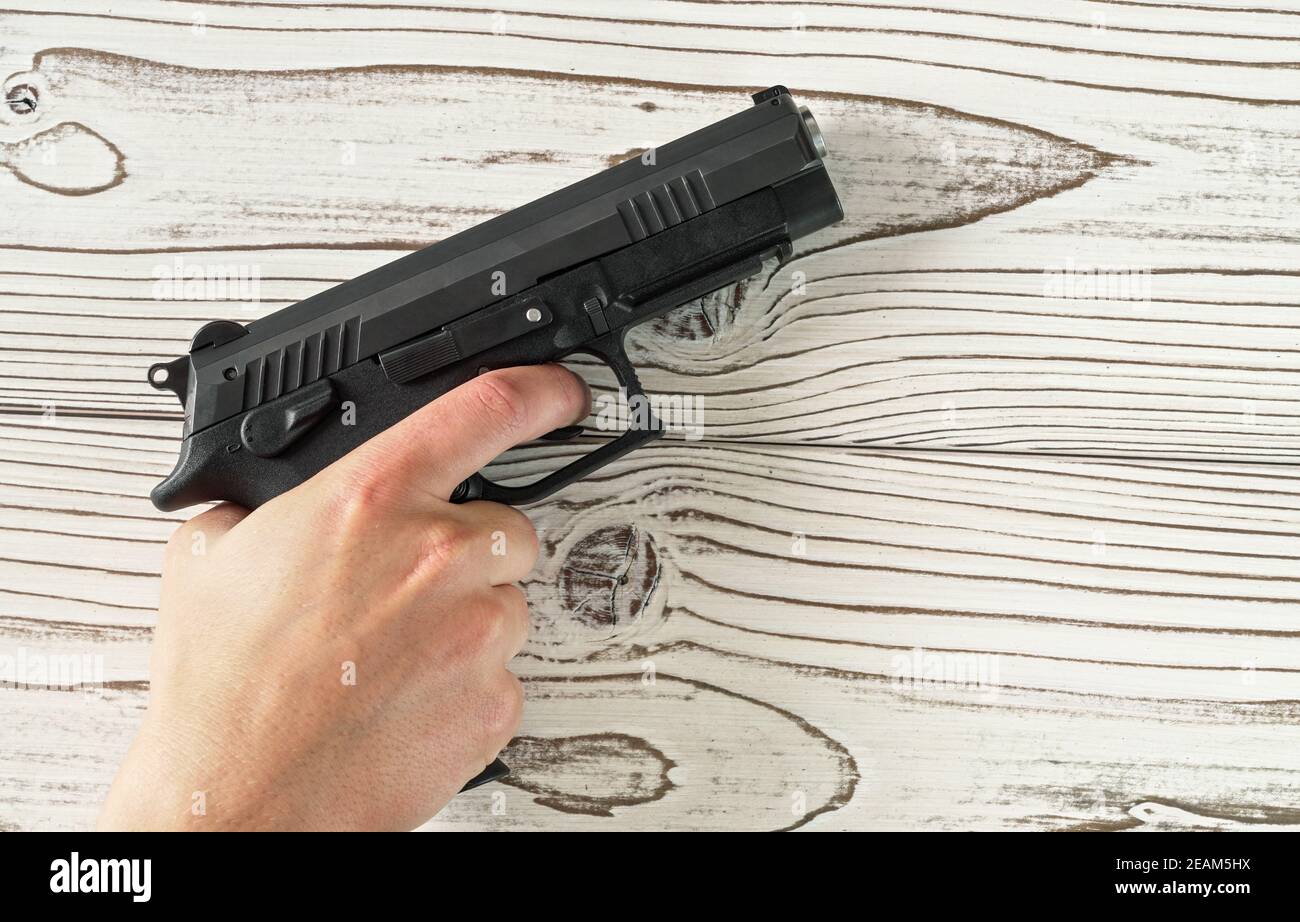 Man hand holding black modern metal gun on white wooden table, closeup ...