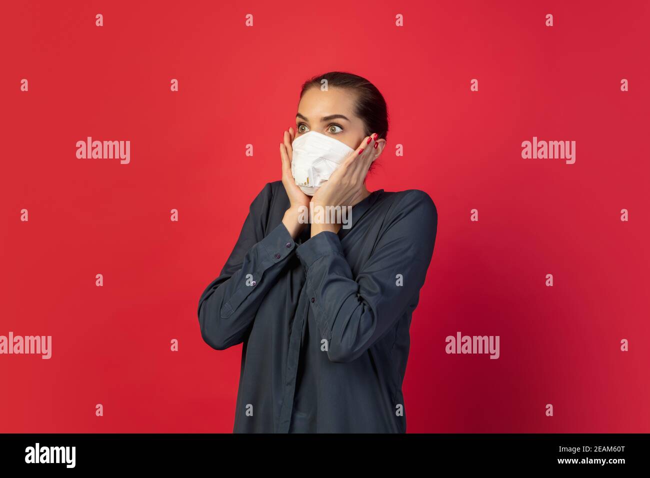 Shocked, scared. Woman in protective face mask isolated on red studio ...
