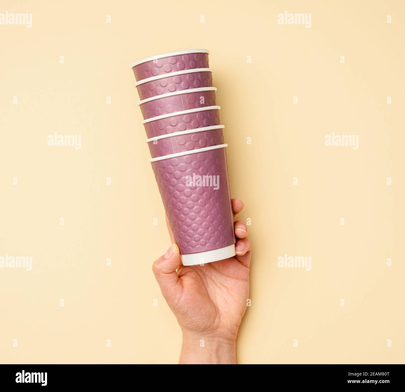 female hand holding stack of purple disposable paper cups on beige ...