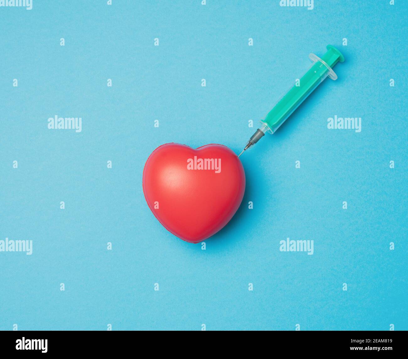 red heart and stuck needle of a plastic syringe inside of it on a blue ...