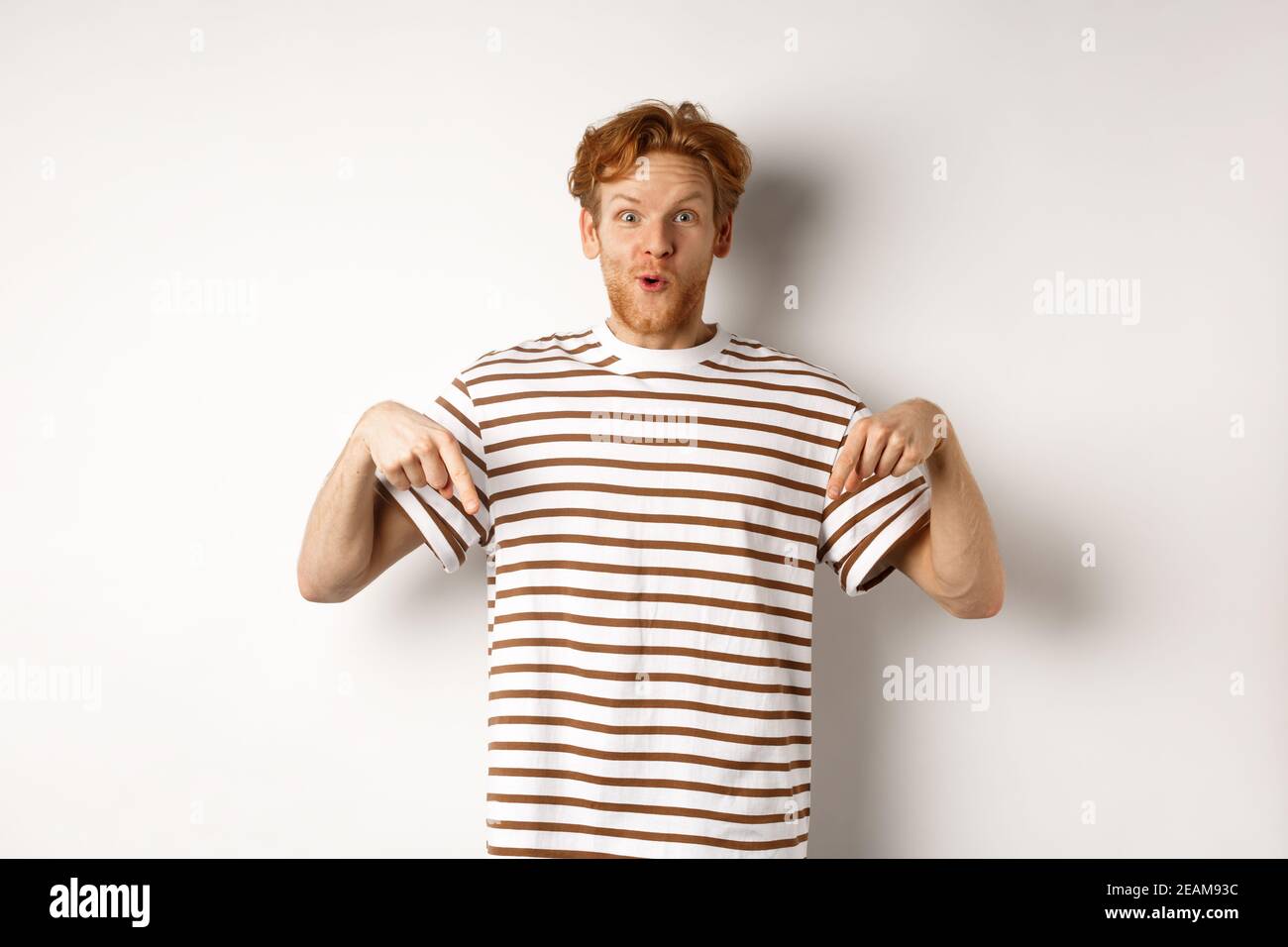 Image of funny redhead male student pointing fingers down, showing ...