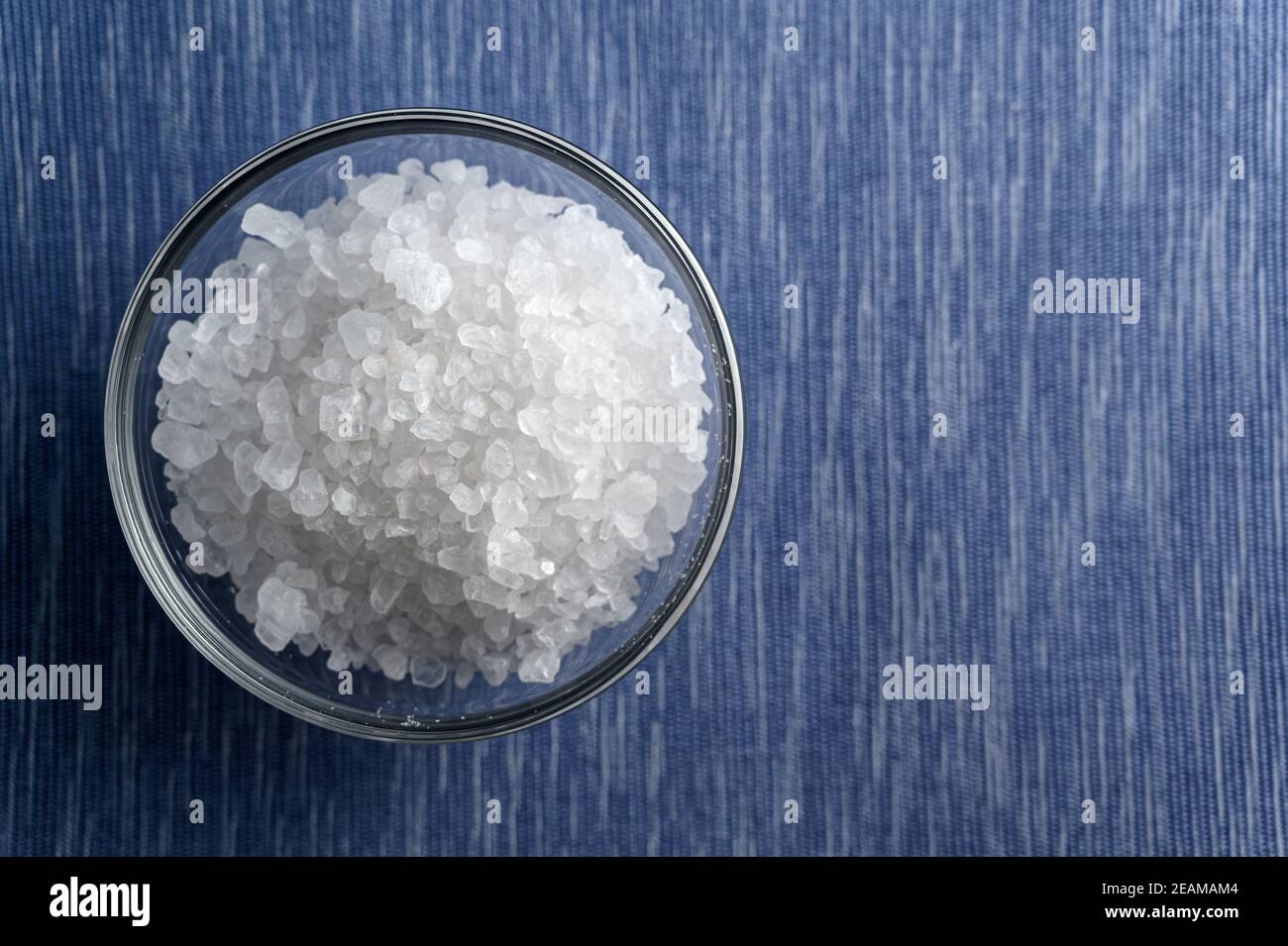 Glass bowl of sea salt on blue background with empty space. Shallow ...