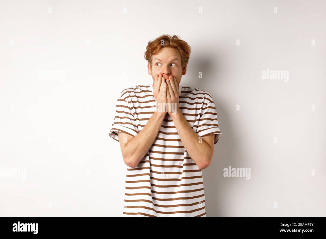 Shocked redhead guy gossiping, giggle in hands and looking left ...