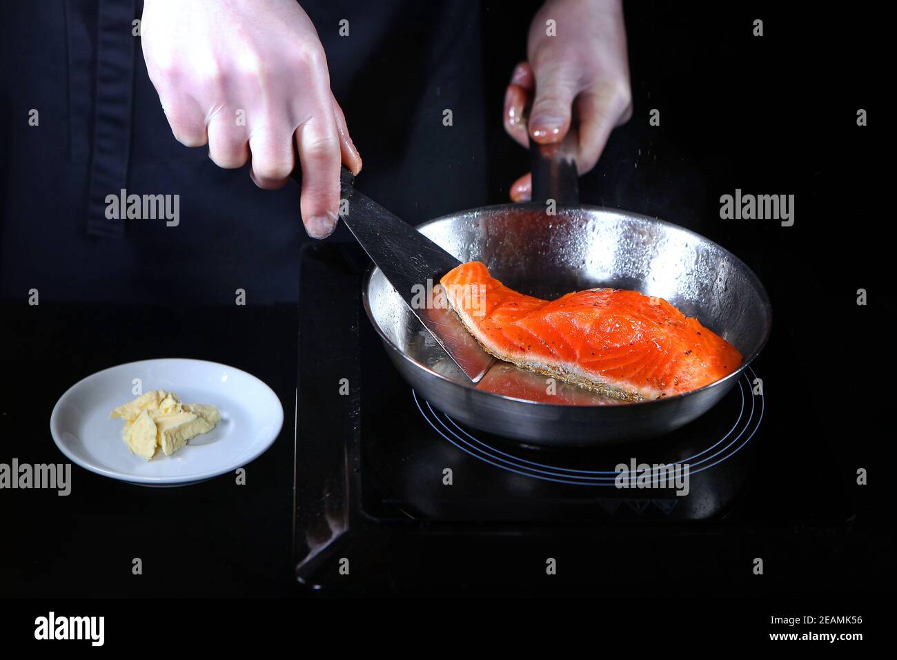 Chef roasts a piece of red fish in a pan. Photo on a black background ...