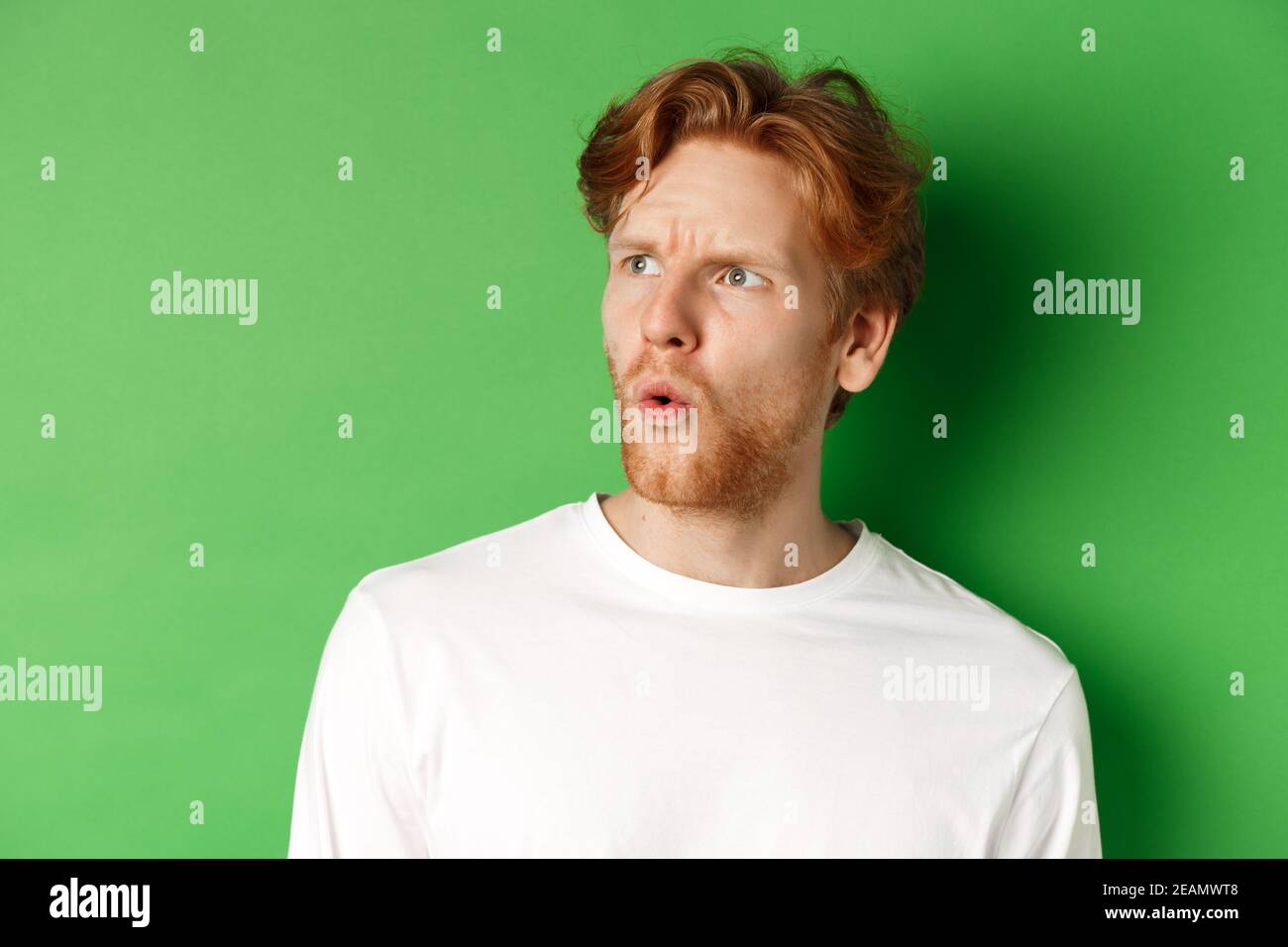 Confused redhead man staring left and looking worried, standing against ...