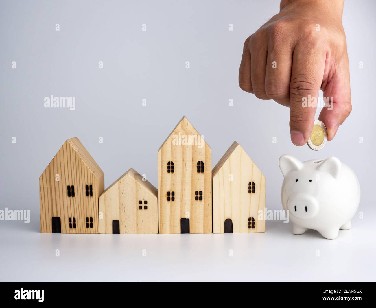 A model wooden house and a man's hand holding a coin On a white ...