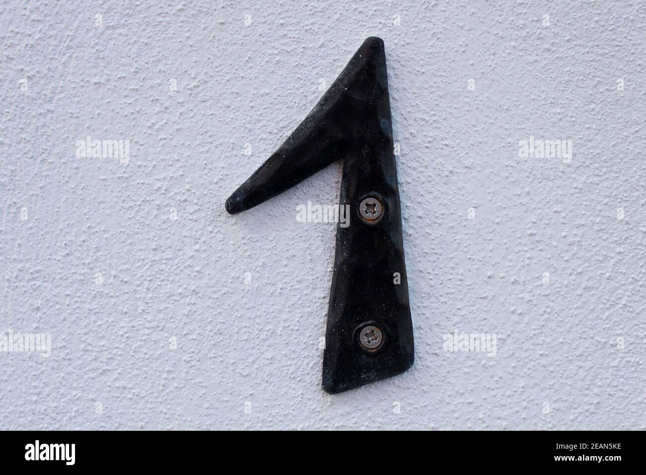 The number 1 carved in wood, painted black and screwed to a white rough ...