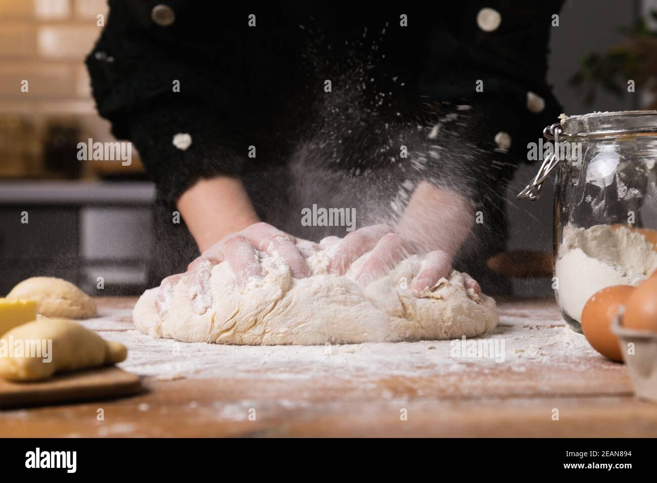 Young beautiful woman kneading dough at a wooden table in kitchen ...