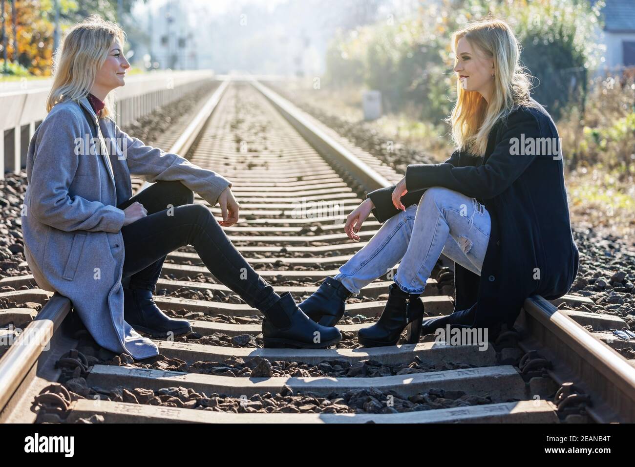 Two attractive young women are sitting on rail and looking at each ...