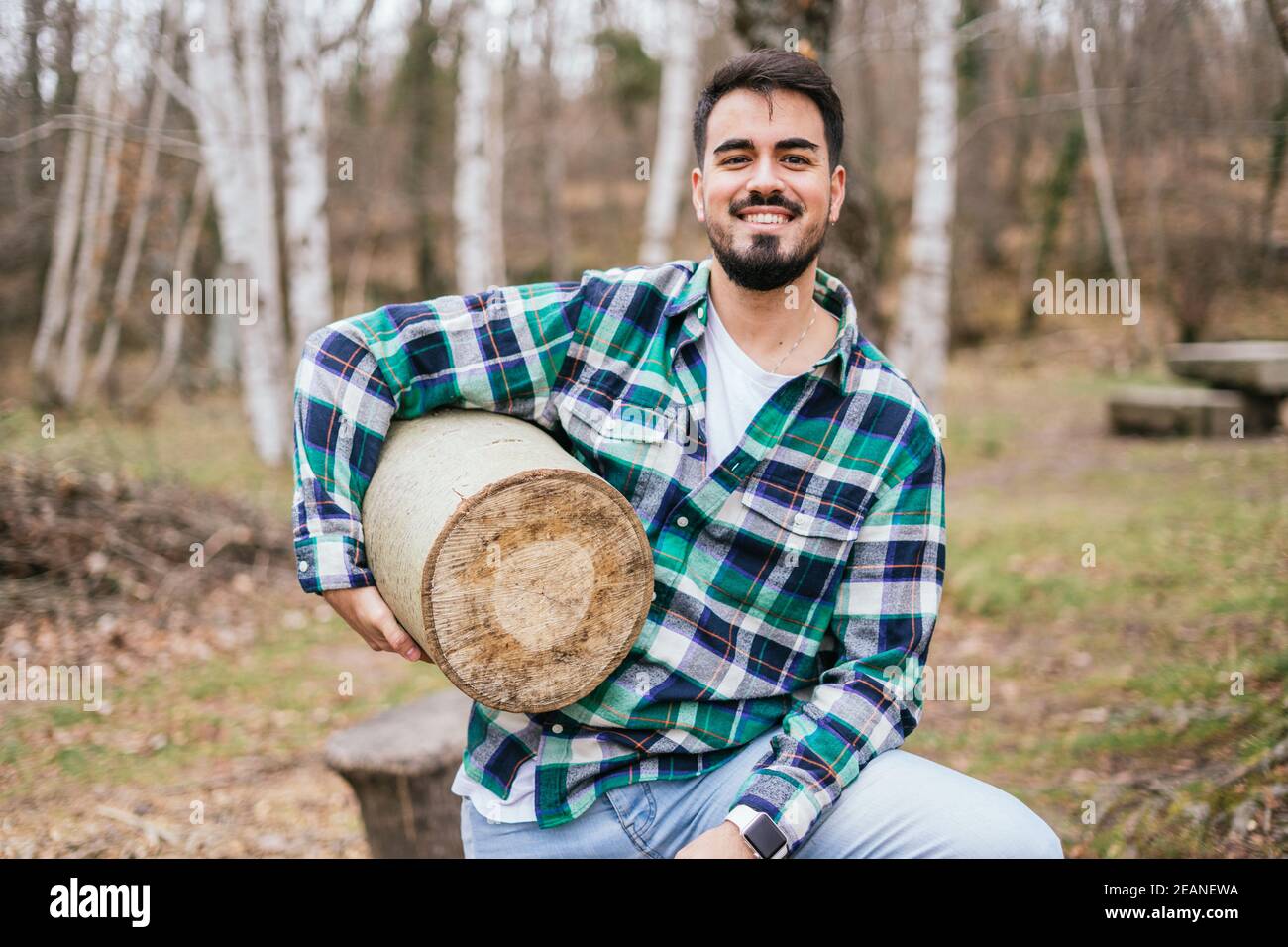 Young Caucasian male with a beard carrying a tree trunk in a forest ...