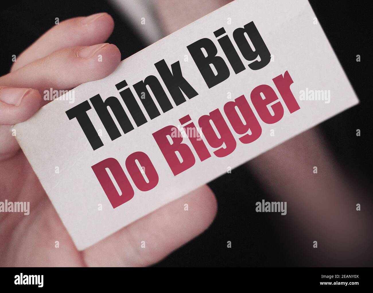 Think Big, Do Bigger. Motivation quote. Businessman holding a card with ...