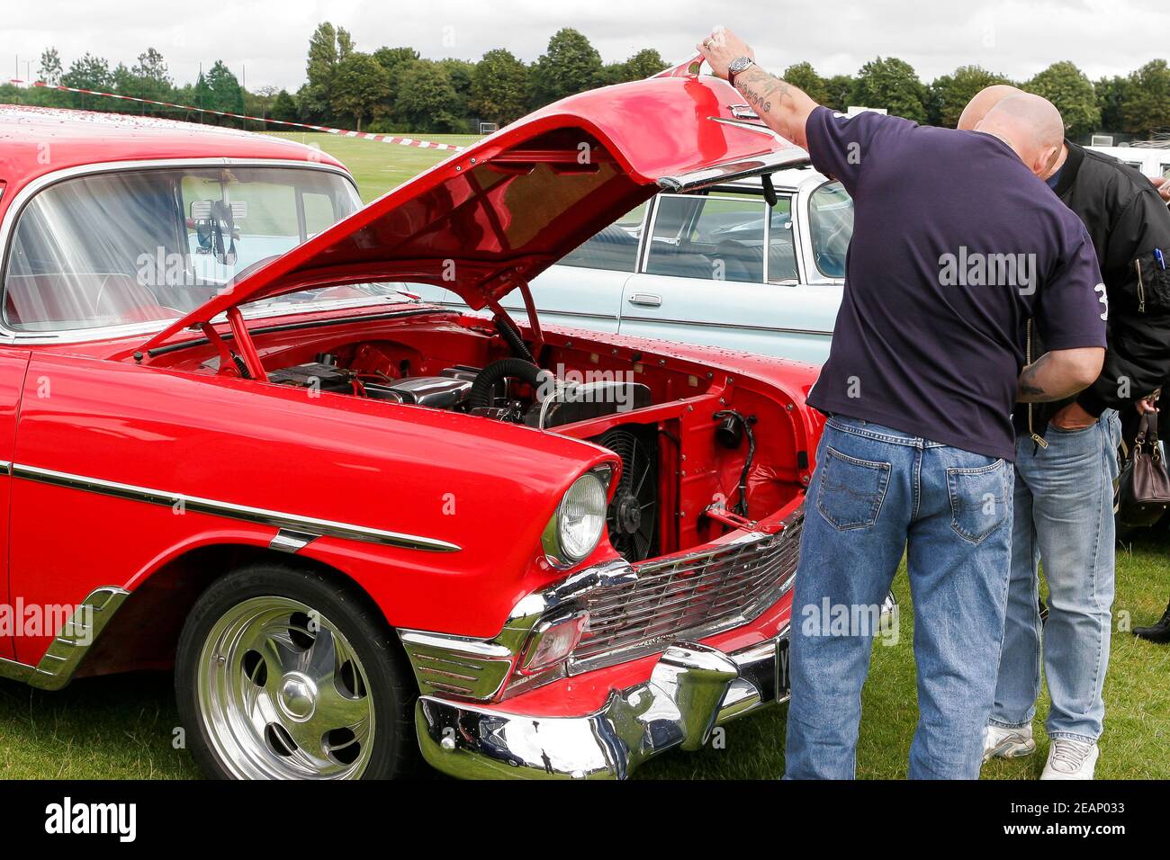 Two men looking under the bonnet at the engine of a red Chevrolet at a ...