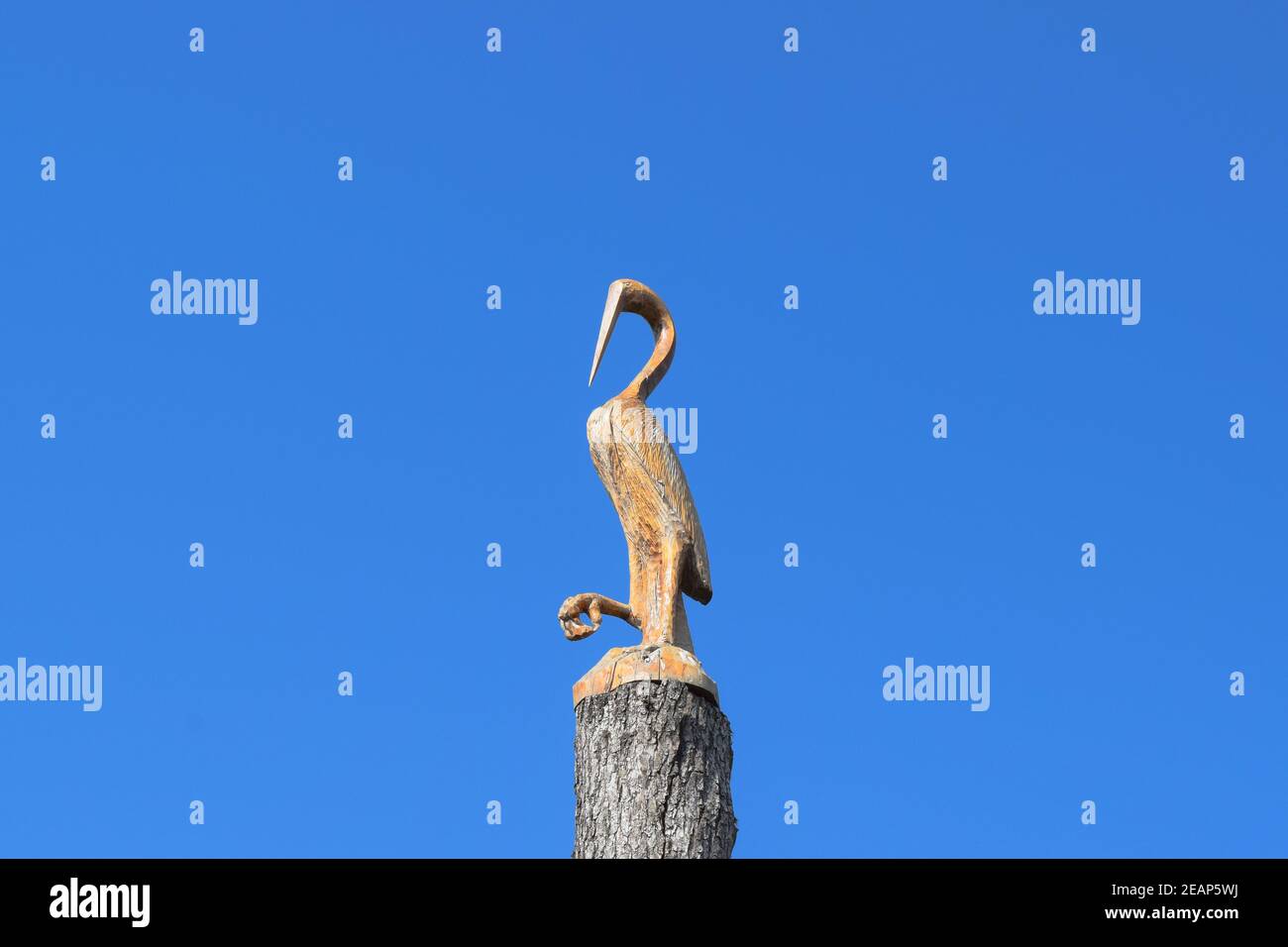 Figure of crane on the stump of a tree against the blue sky. Figures of ...