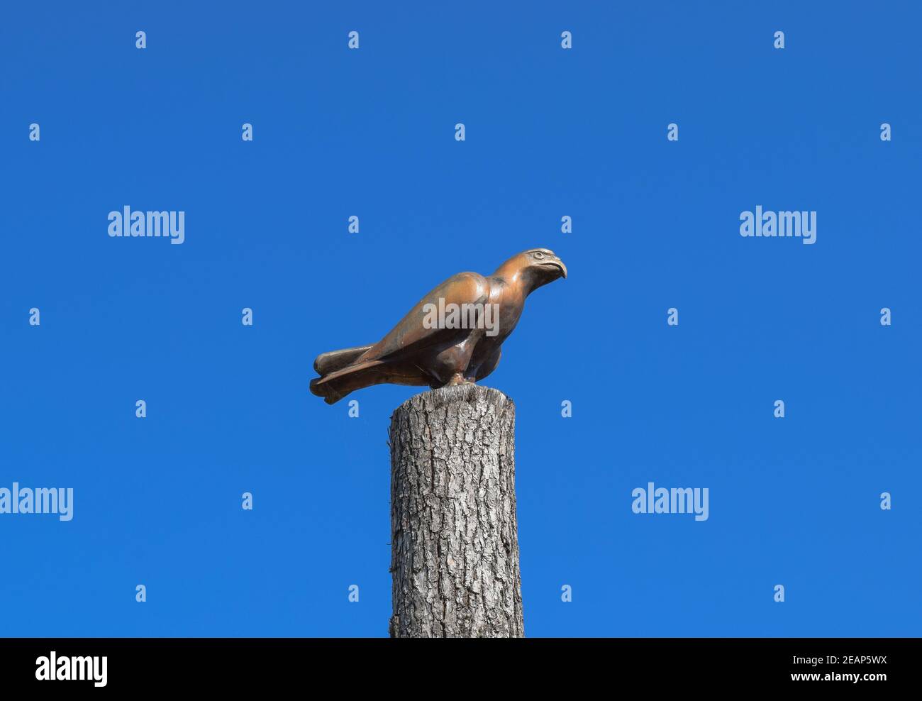 Figurine of a falcon on a stump of a tree against the blue sky. Figures ...