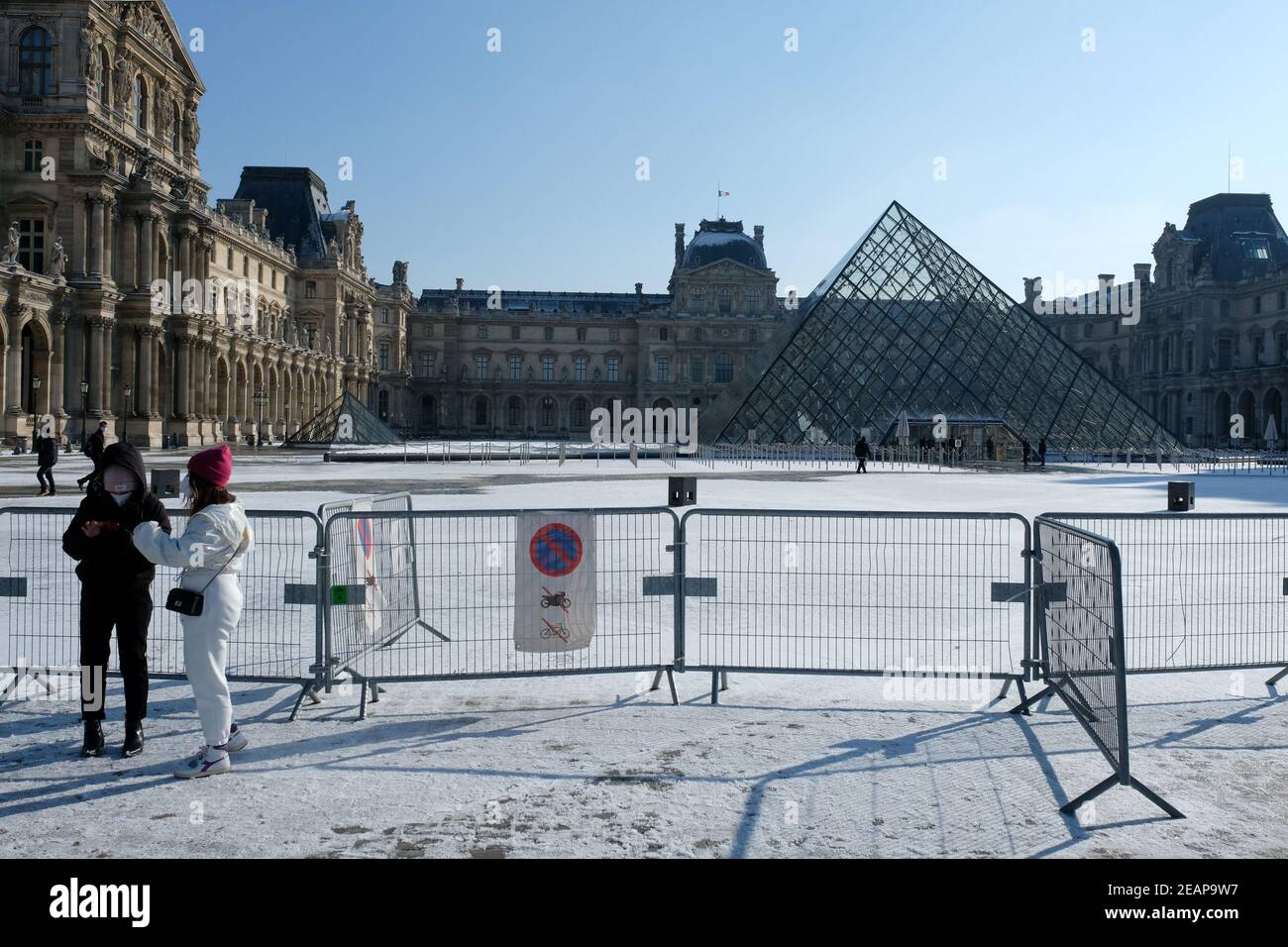 Two woman taking pictures in front of the snow-covered Louvre Museum ...