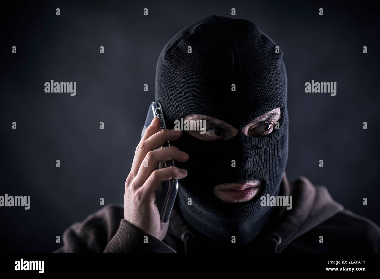 Criminal wearing black balaclava and hoodie with a smartphone in the ...
