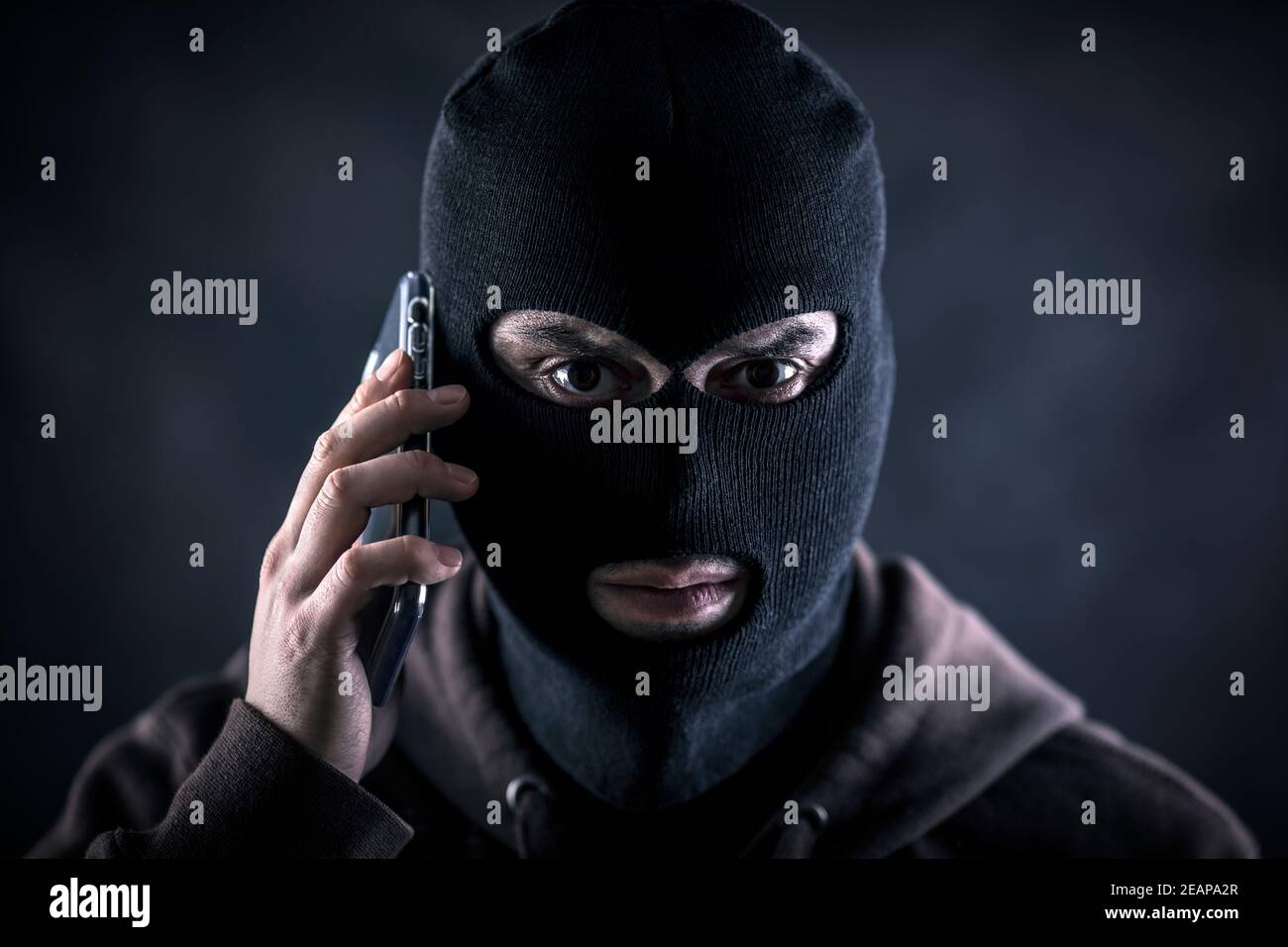 Criminal wearing black balaclava and hoodie with a smartphone in the ...