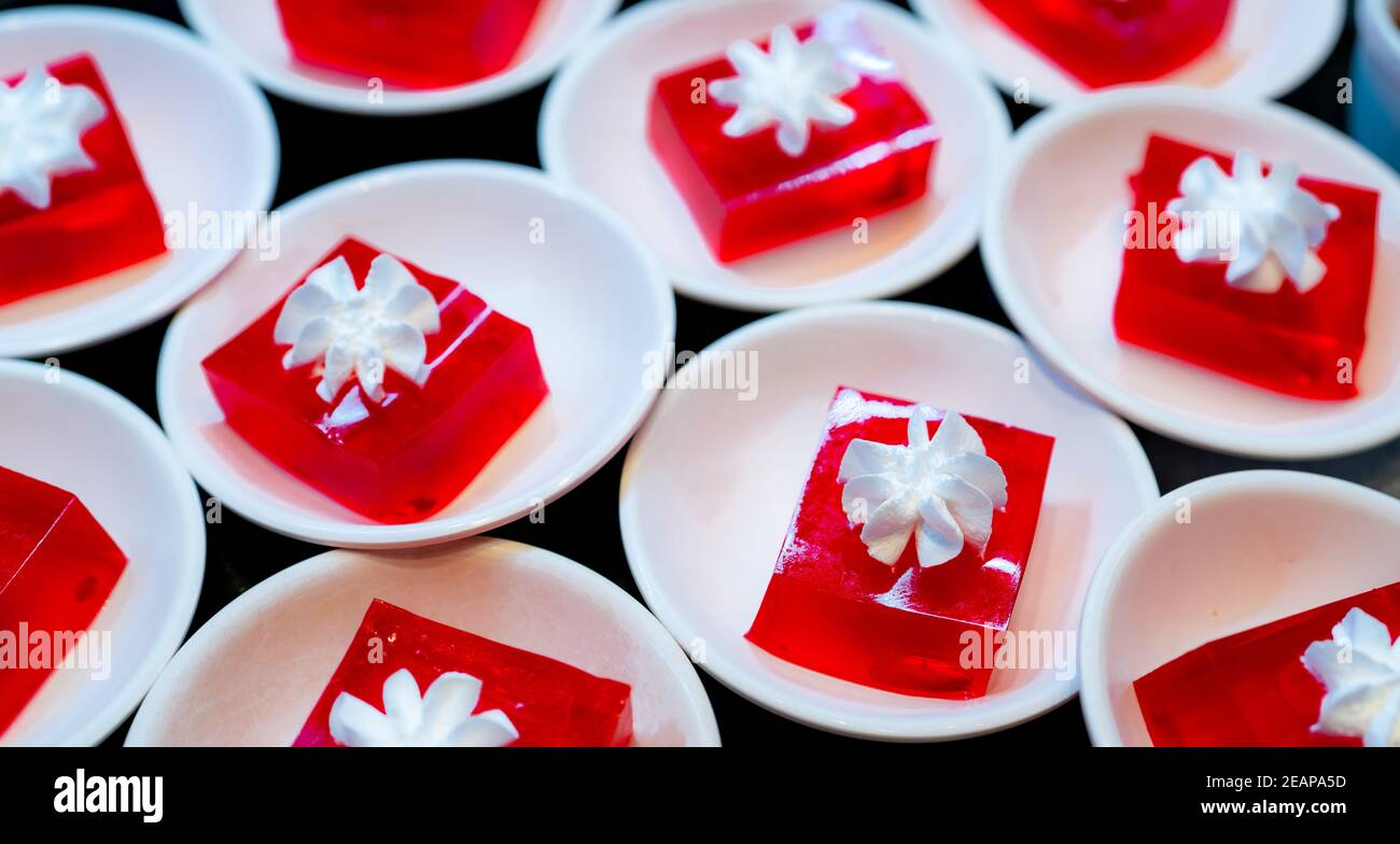 Red jelly dessert with whipped cream served on white plate. Square red ...