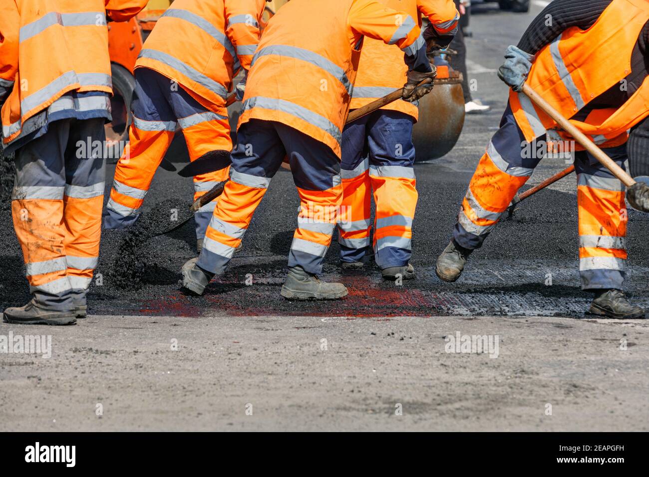 A team of road workers in orange reflective uniforms use shovels to ...