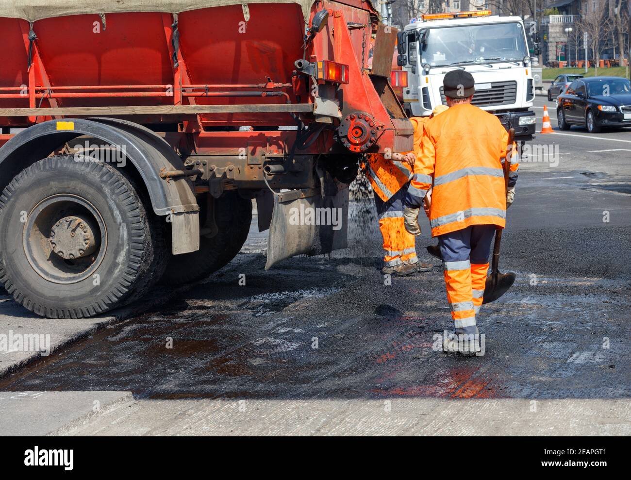 A team of road workers with a hot asphalt truck repairing a section of ...