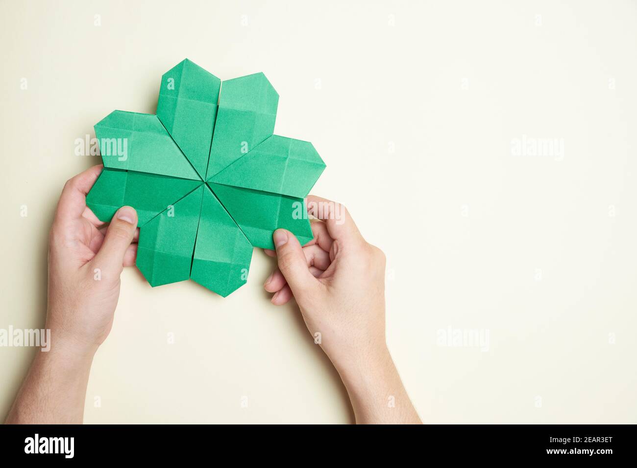 Origami four-leaf clover, made of green paper, held by two hands of ...