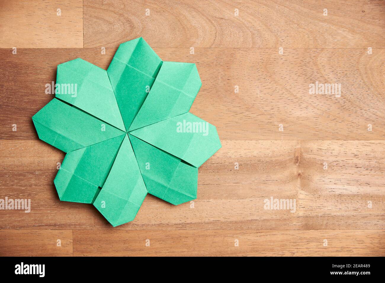 Origami four-leaf clovers, made of green paper, on a wooden background ...