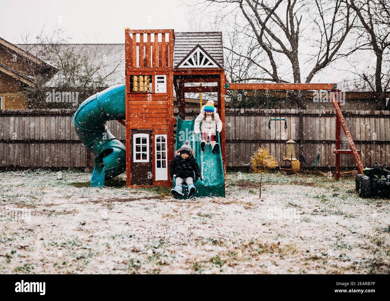 Young brother and sister sliding down swing set with falling snow Stock ...