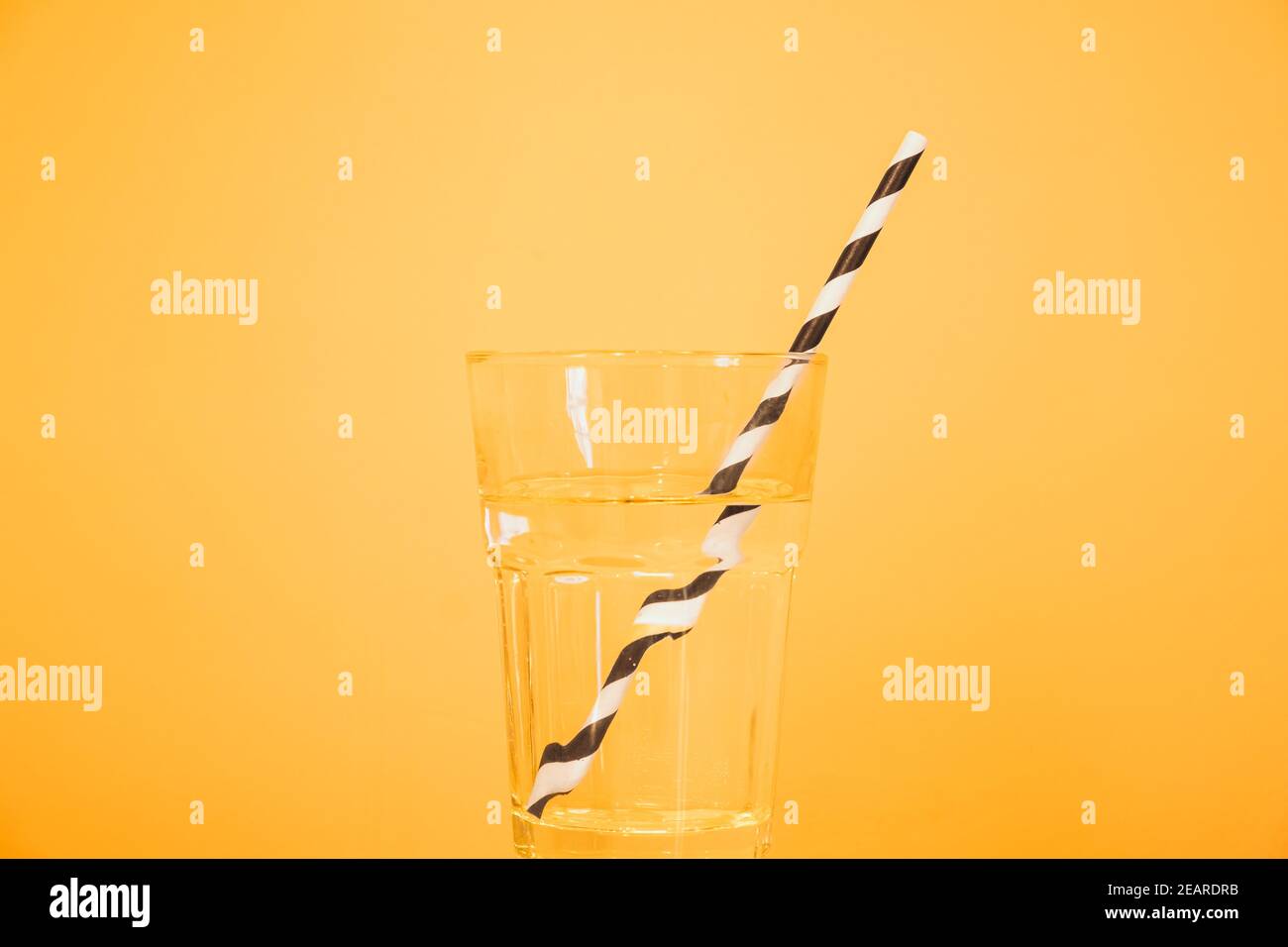 Drinking straw in a glass of water, bright yellow orange studio ...